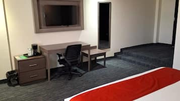 Quarto de hotel com cama, escrivaninha, cadeira e televisão fixada na parede.
