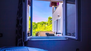 Quarto com uma grande janela, uma cama e vista para uma varanda com mobiliário exterior.