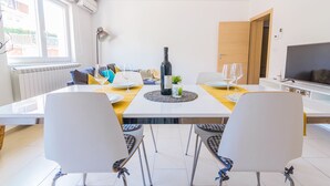 Uma sala de estar moderna com uma mesa de jantar posta para dois, um sofá, uma TV e uma janela com um aparelho de ar condicionado.