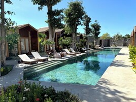 Uma área junto à piscina com espreguiçadeiras, piscina cristalina e vegetação ao redor.
