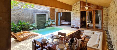 Uma área moderna para refeições ao ar livre com piscina, móveis de madeira e uma parede de pedra.