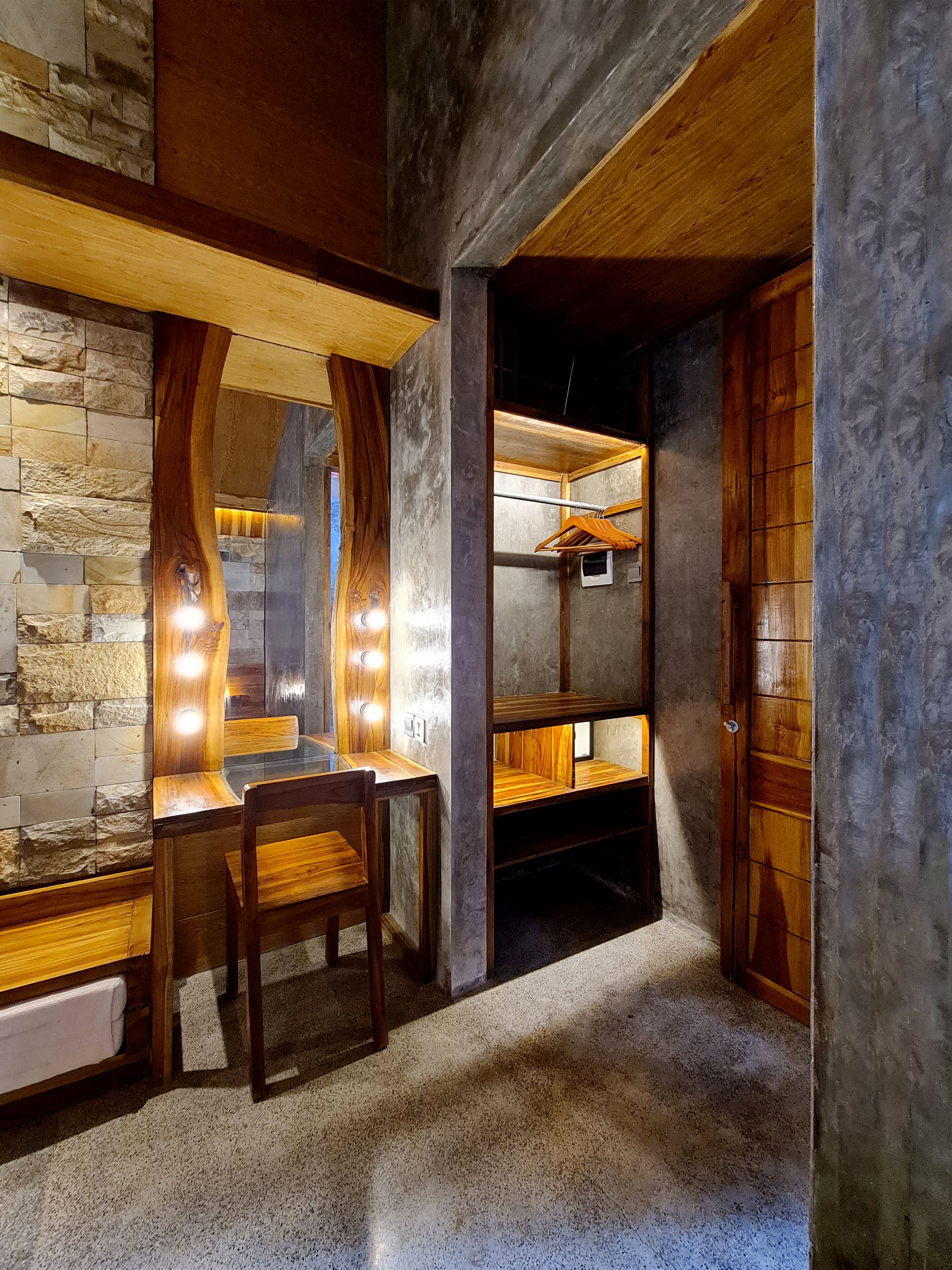 Quarto com parede de pedra, mobiliário de madeira e um espelho refletindo a luz.