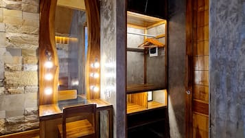 Quarto com parede de pedra, mobiliário de madeira e um espelho refletindo a luz.