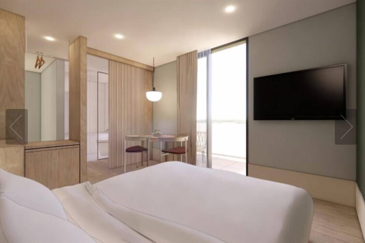 Quarto de hotel moderno com uma cama grande, uma escrivaninha com duas cadeiras, uma televisão de tela plana na parede e uma varanda com vista.