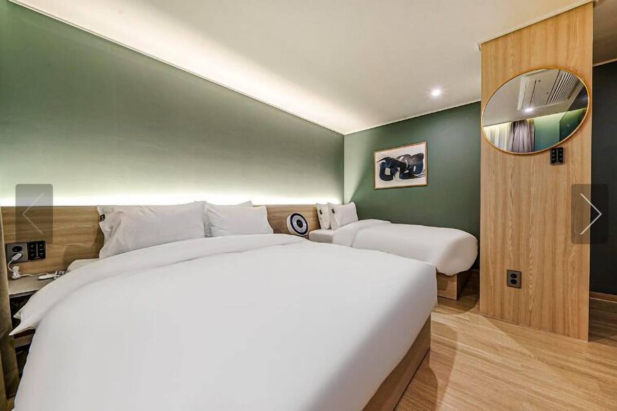 Quarto de hotel moderno com uma cama grande, um guarda-roupa de madeira, um espelho redondo e um quadro emoldurado na parede.