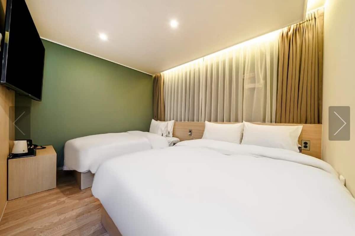 Quarto de hotel com duas camas, televisão de tela plana, mesa de cabeceira e janela com cortina.