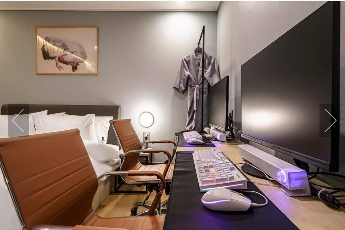 Quarto de hotel moderno com uma cama, uma escrivaninha com computador, uma cadeira e uma televisão de tela plana grande.