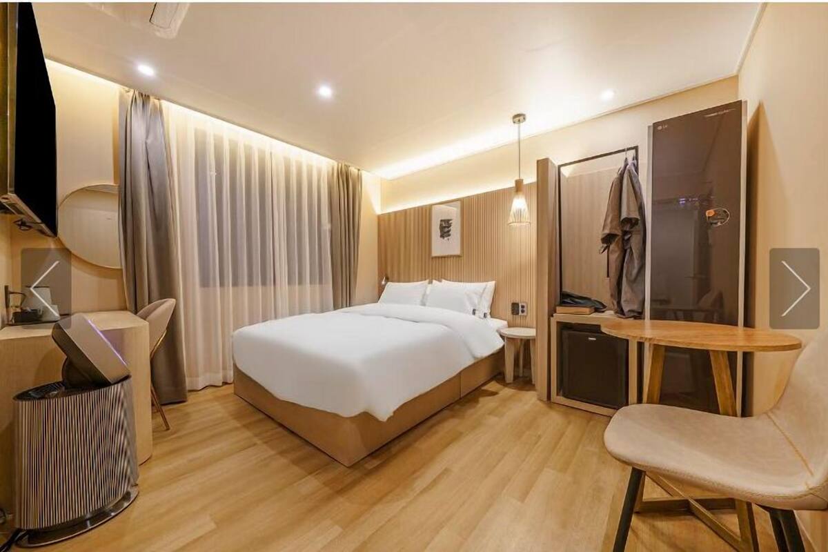 Quarto de hotel moderno com cama, escrivaninha, cadeira, espelho e chuveiro.