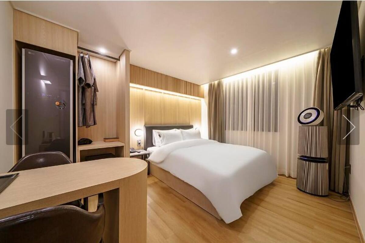 Quarto de hotel com cama, escrivaninha, cadeira, guarda-roupa e televisão.
