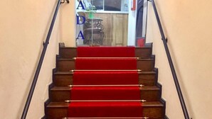 Escadaria com degraus revestidos de carpete vermelho e corrimãos pretos.