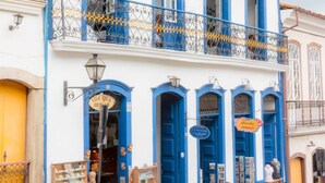 Um edifício com portas e janelas azuis, uma varanda com grades de metal e uma placa que diz "Vila Rica".
