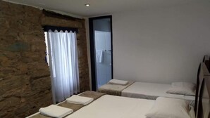 Quarto com quatro camas dispostas em linha, uma parede de pedra e uma porta para um banheiro.