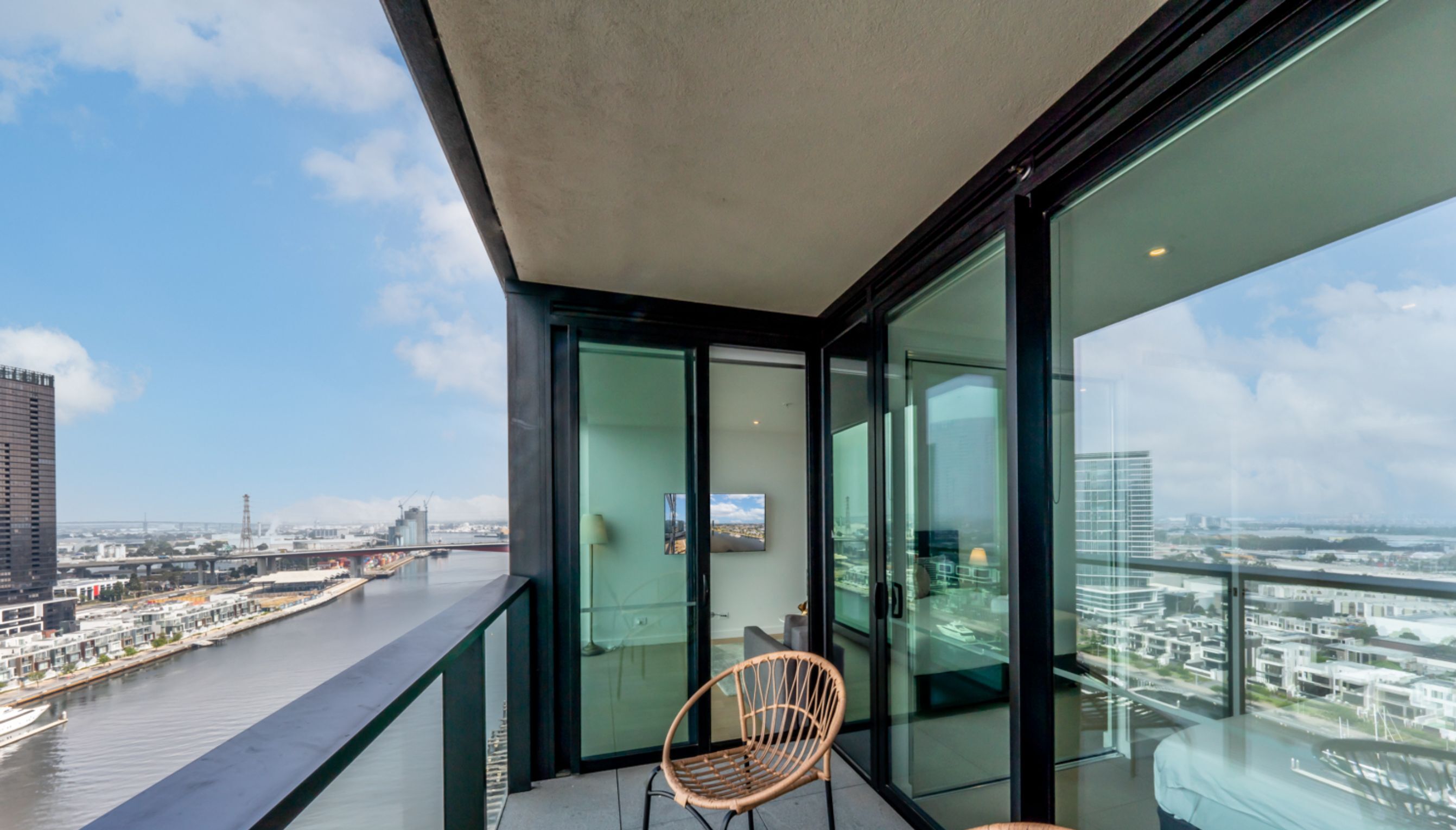 Uma varanda moderna com porta de vidro, uma cadeira de vime e vista para a cidade.