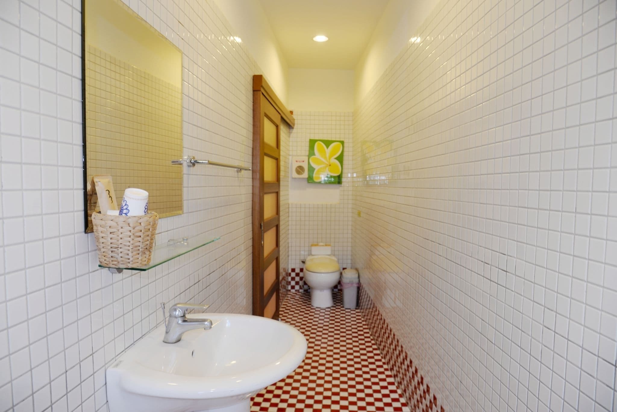 Um banheiro pequeno com paredes de azulejos brancos, chão quadriculado, pia, espelho e vaso sanitário.