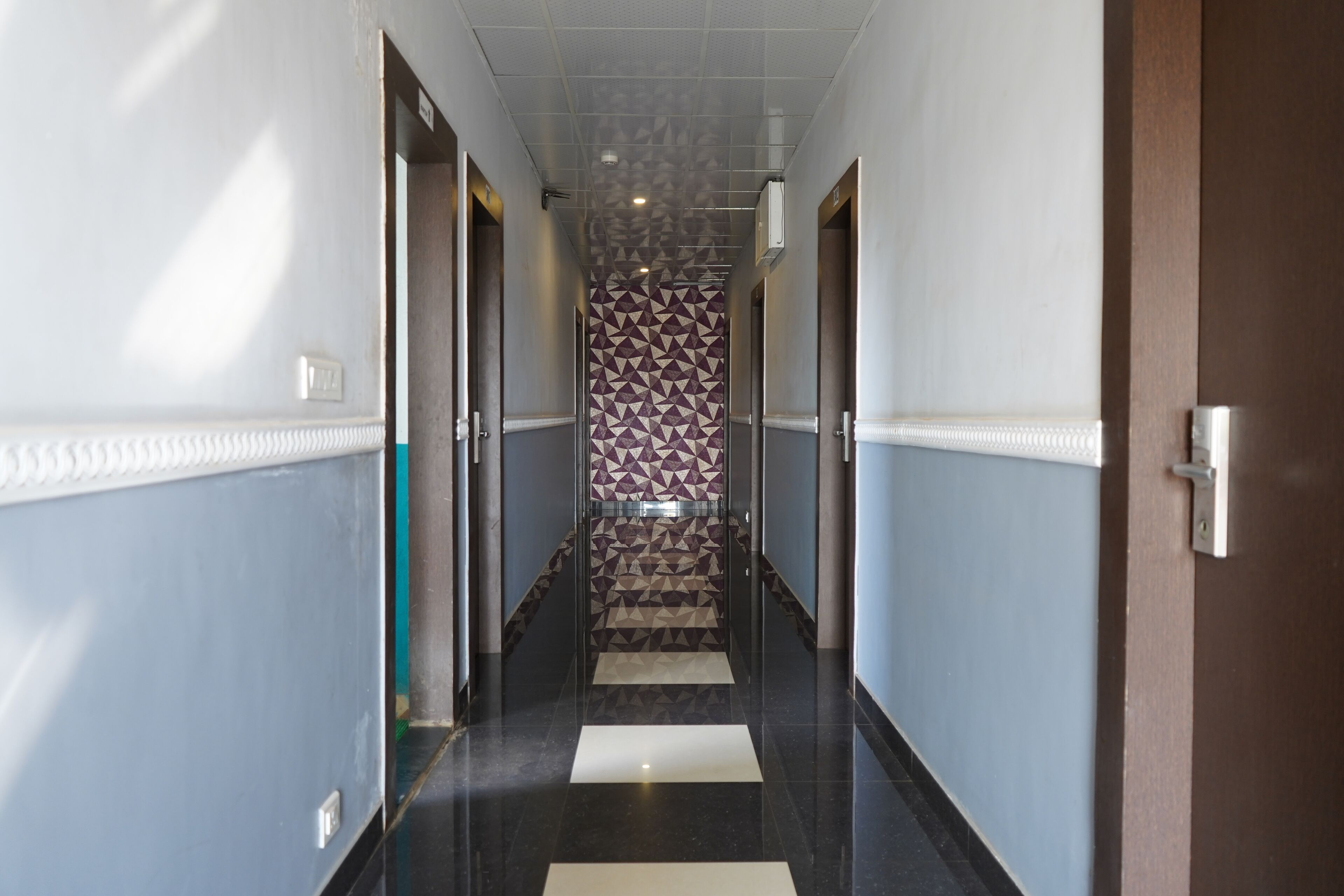 Um corredor com paredes estampadas, portas de ambos os lados e piso ladrilhado.