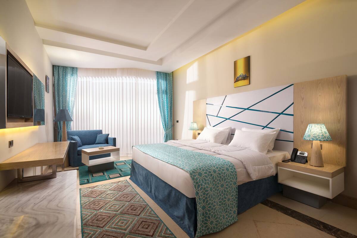 Quarto de hotel com cama, mesa de cabeceira, abajur e televisão.