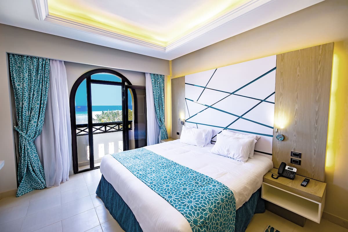 Quarto de hotel com uma cama grande, telefone de cabeceira, mesa de apoio e vista para o oceano através de uma janela ampla.