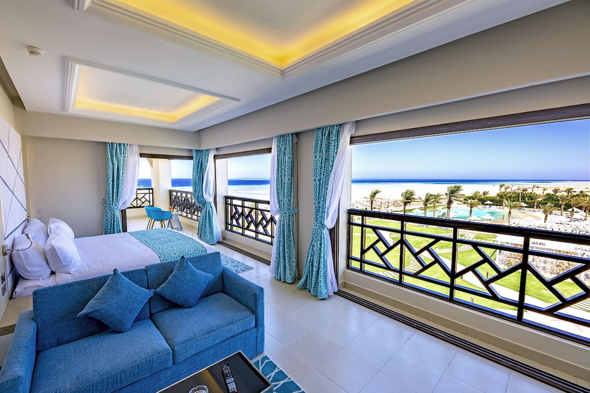 Quarto de hotel com varanda, uma cama, um sofá azul e vista para a praia.