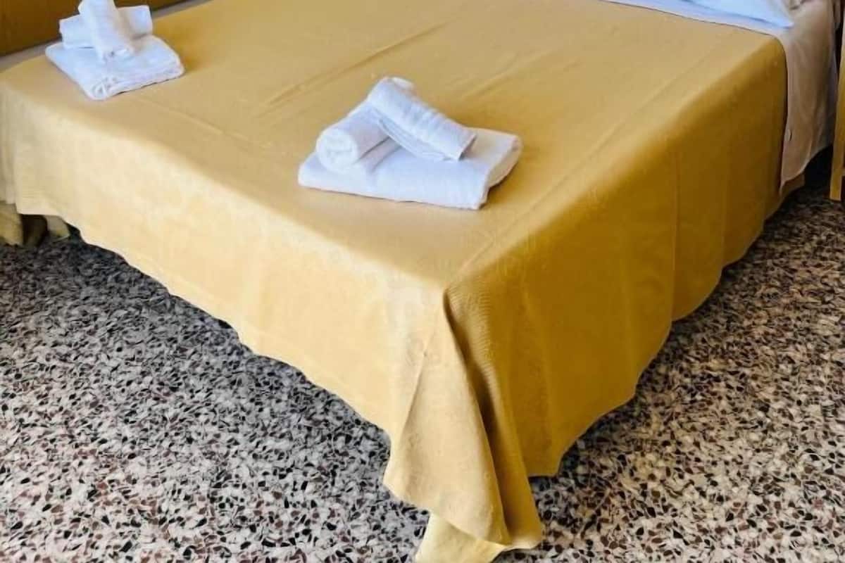 Quarto de hotel com uma cama, mesa de cabeceira, espelho e chão coberto de carpete.