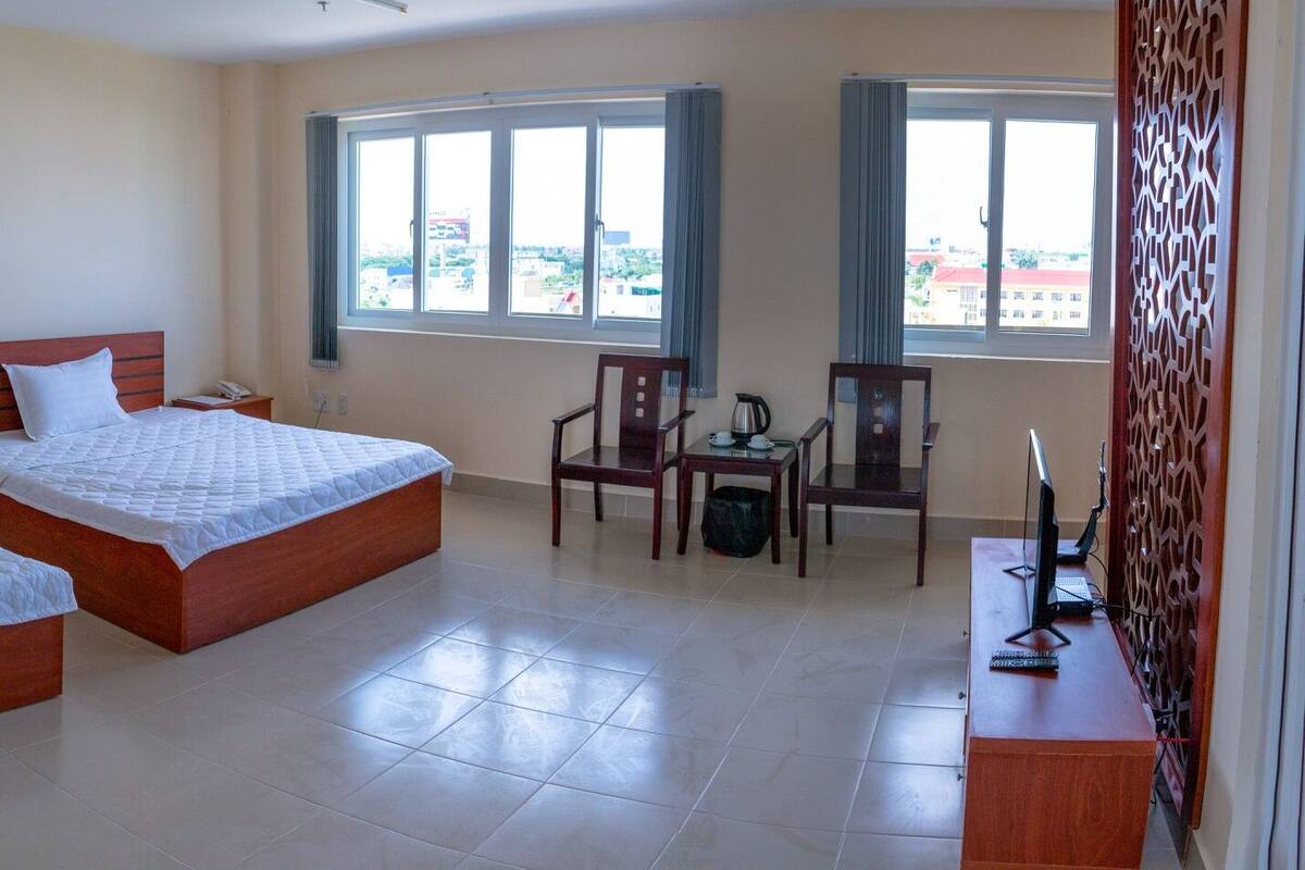 Quarto de hotel com duas camas, uma escrivaninha, uma cadeira, uma mesinha com chaleira e uma janela com vista.