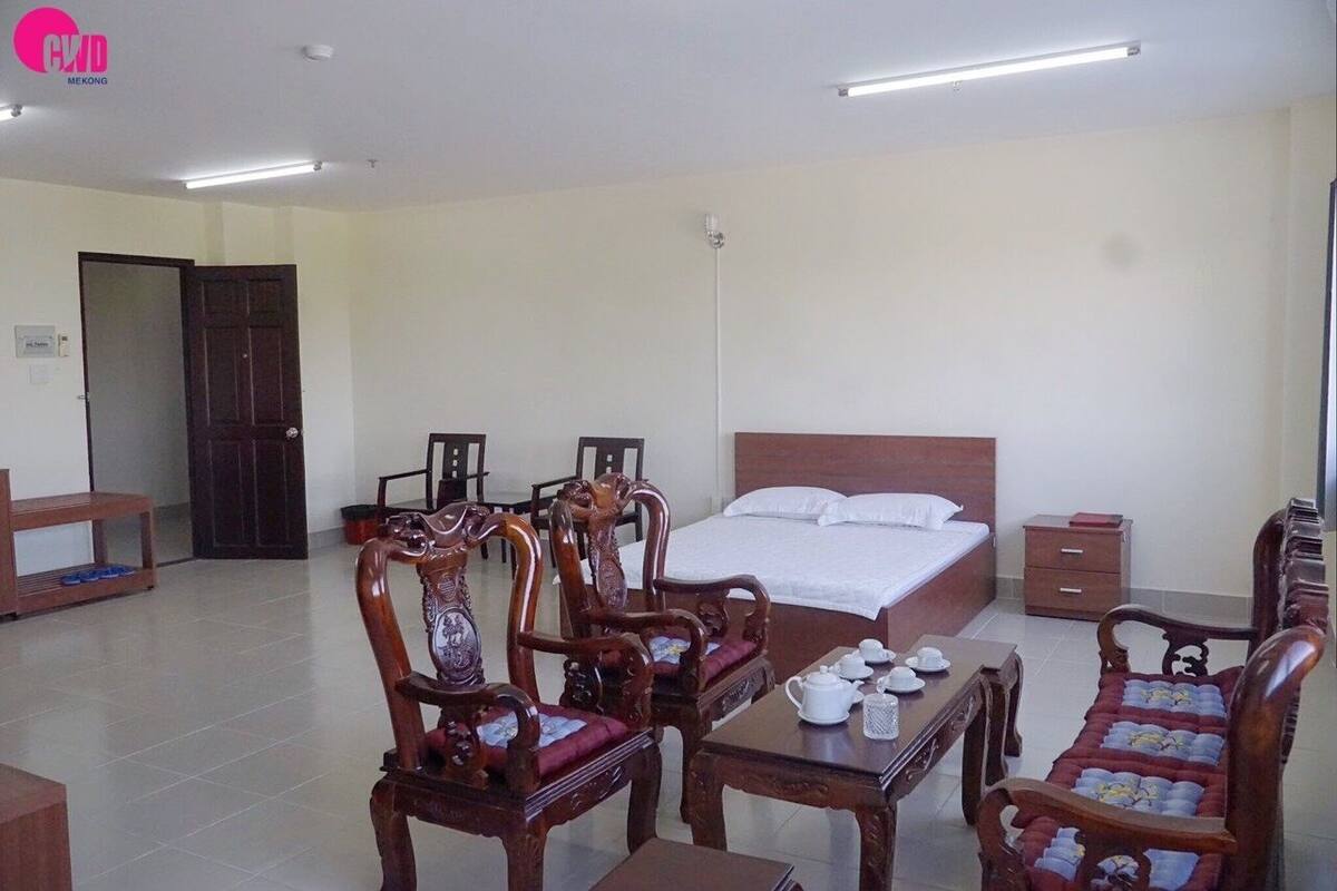 Quarto de hotel com uma cama, cadeiras de madeira, uma mesa com jogo de chá e um guarda-roupa.