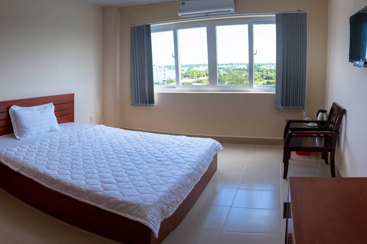 Quarto com cama, mesa de cabeceira, escrivaninha e janela com cortinas.