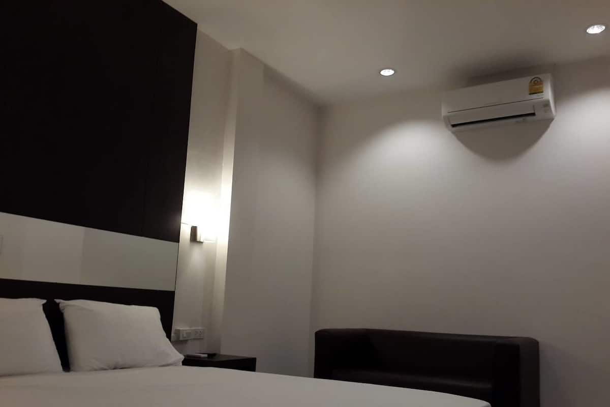 Quarto de hotel com cama, mesa de cabeceira, cadeira e ar condicionado.