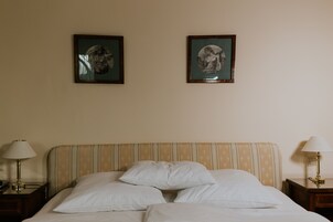 Uma cama bem arrumada com lençóis brancos, duas luminárias de cabeceira e duas obras de arte emolduradas na parede.