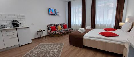 Quarto de hotel moderno com cama, sofá, pequena cozinha e televisão.