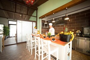 Uma cozinha moderna com um chef, um balcão extenso e uma área de jantar com cadeiras brancas.