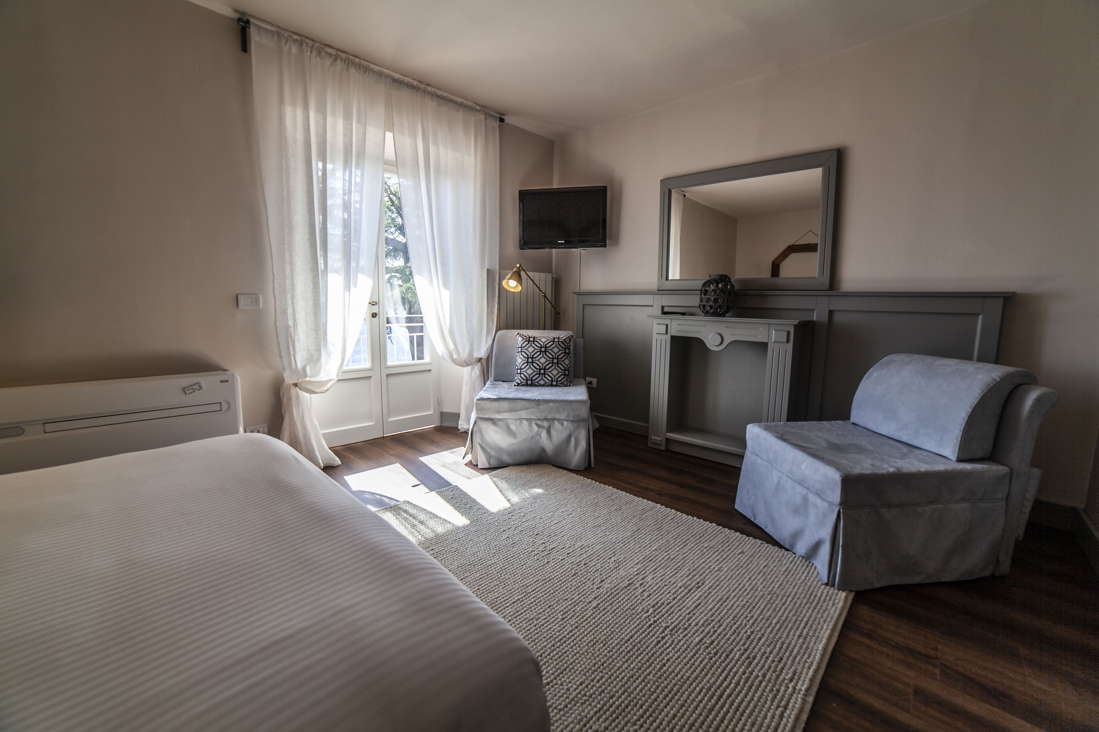 Quarto com uma cama grande, uma escrivaninha com cadeira, televisão e janela com cortinas.
