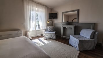 Quarto com uma cama grande, uma escrivaninha com cadeira, televisão e janela com cortinas.