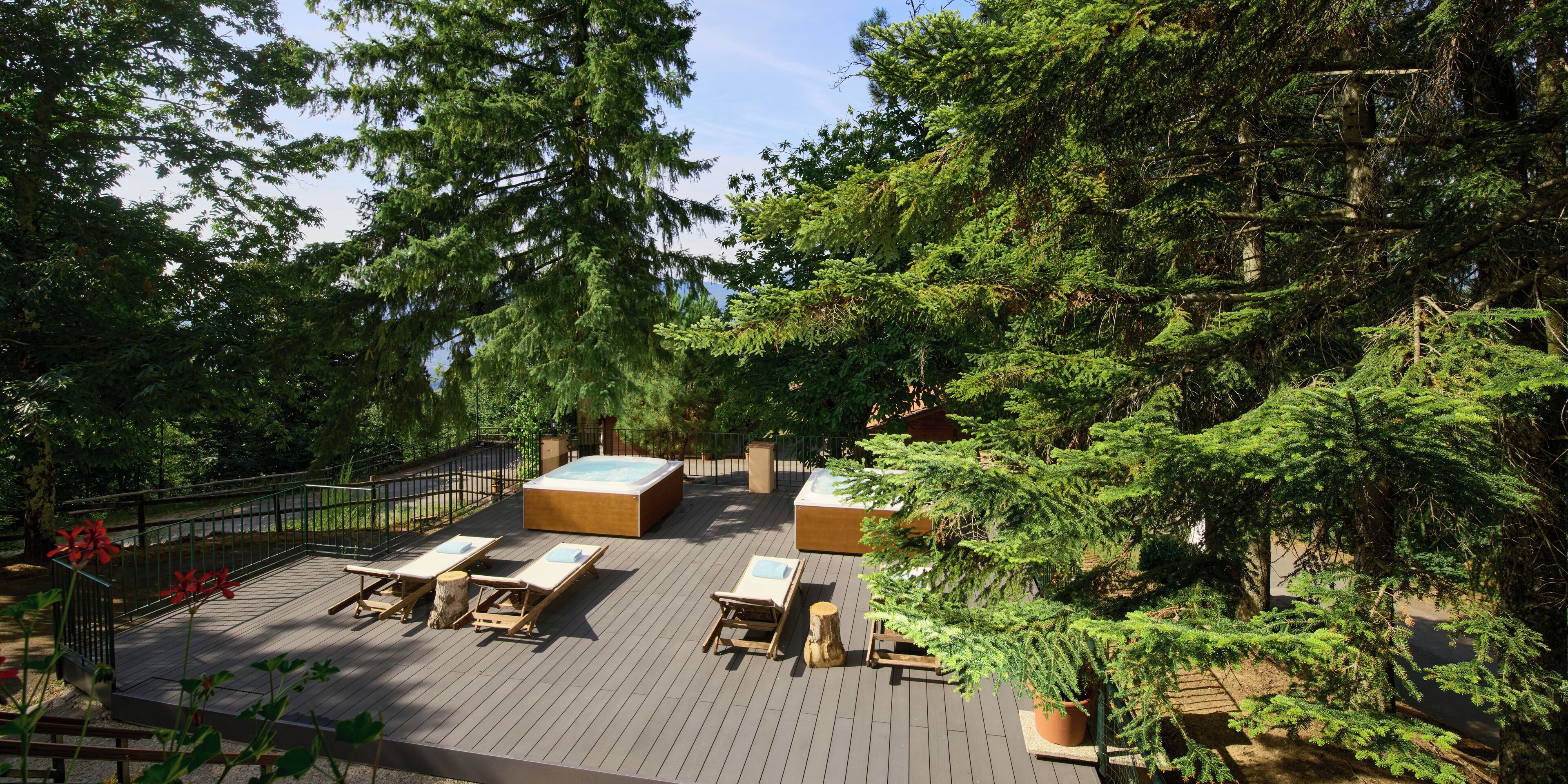 Um terraço com espreguiçadeiras e uma banheira de hidromassagem, cercado por árvores densas.