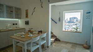 Cozinha moderna com armários brancos, uma mesa de jantar posta para quatro pessoas e vista para a cidade através de uma grande janela.
