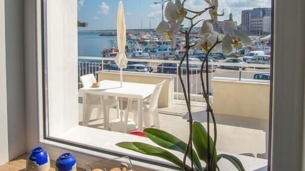 Varanda com vaso de planta, uma mesa pequena e vista para um porto de iates.
