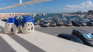 Marina com diversos barcos atracados, área de estacionamento com carros e uma ponte sobre ela.