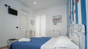 Quarto de hotel com cama, mesa de cabeceira, cadeira, televisão e janela com cortinas.