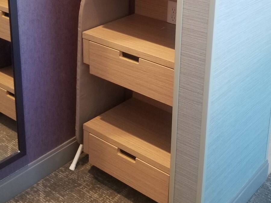 Canto de um quarto com uma estante de madeira encostada a uma parede com painel roxo e azul claro.