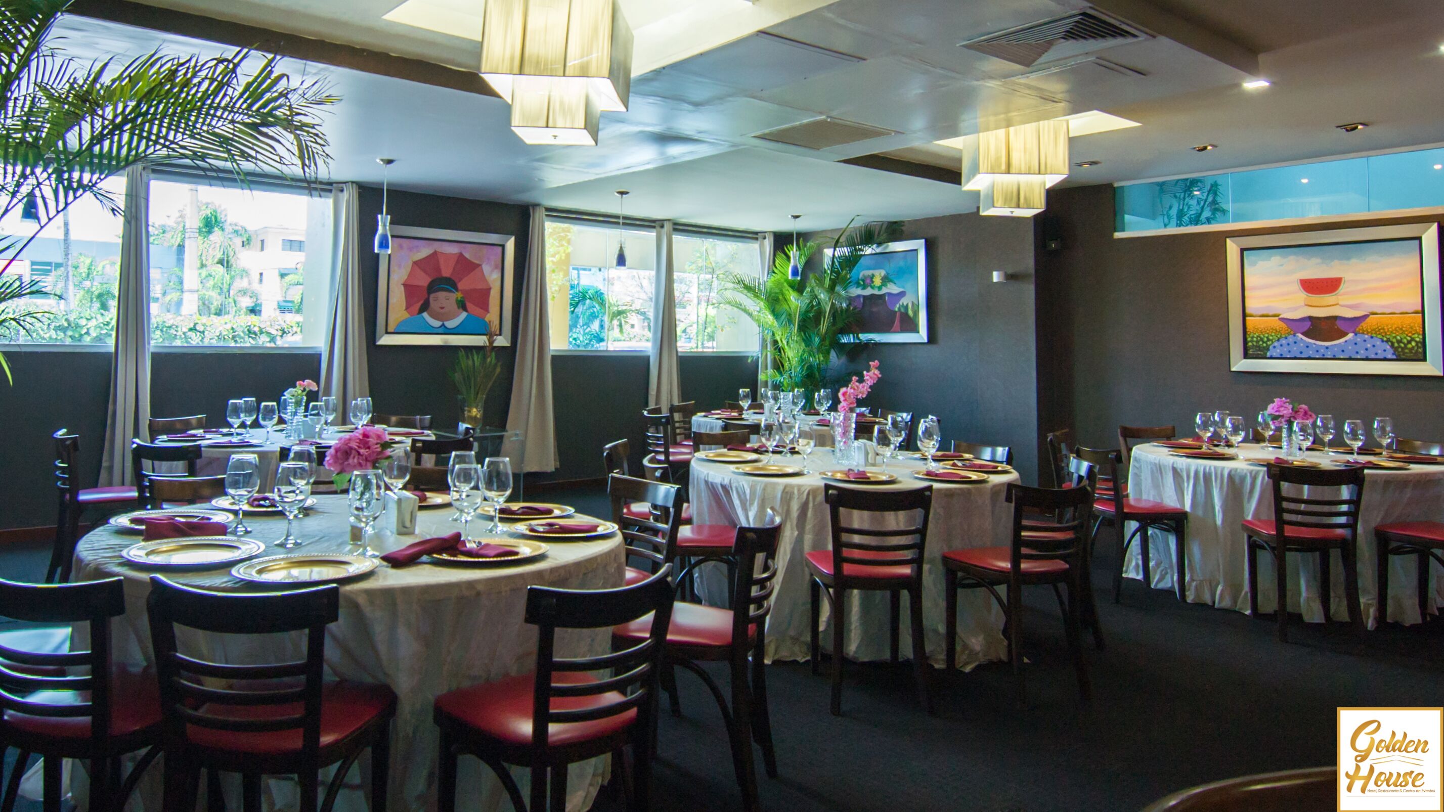 Restaurante com mesas redondas preparadas para refeições, cadeiras e luminárias pendentes.