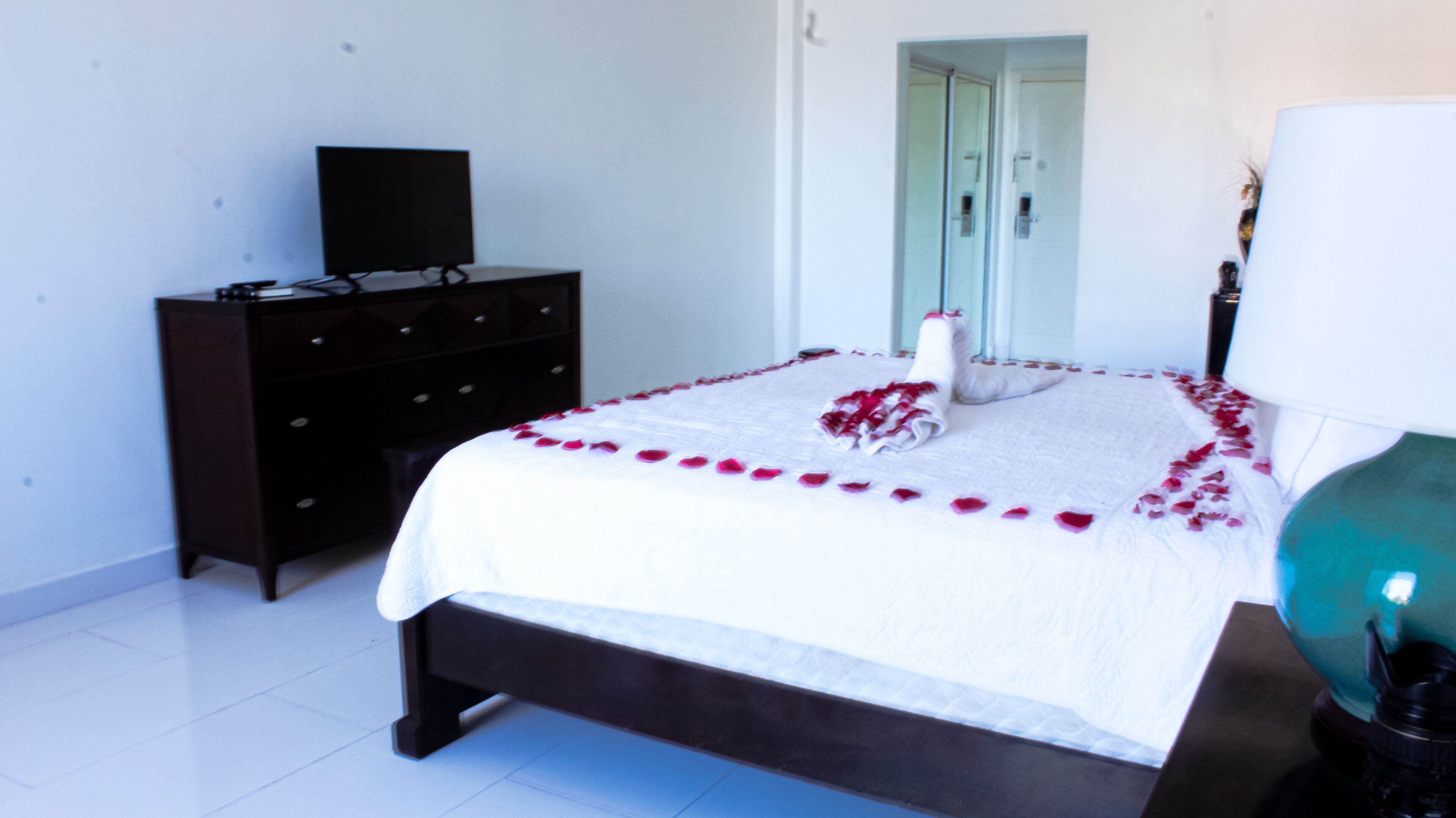 Quarto com cama, cômoda, televisão e espelho.