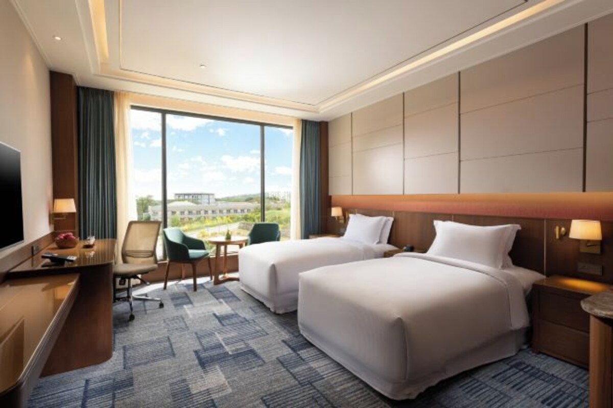 Quarto de hotel com duas camas, uma mesa, televisão e vista para a cidade.