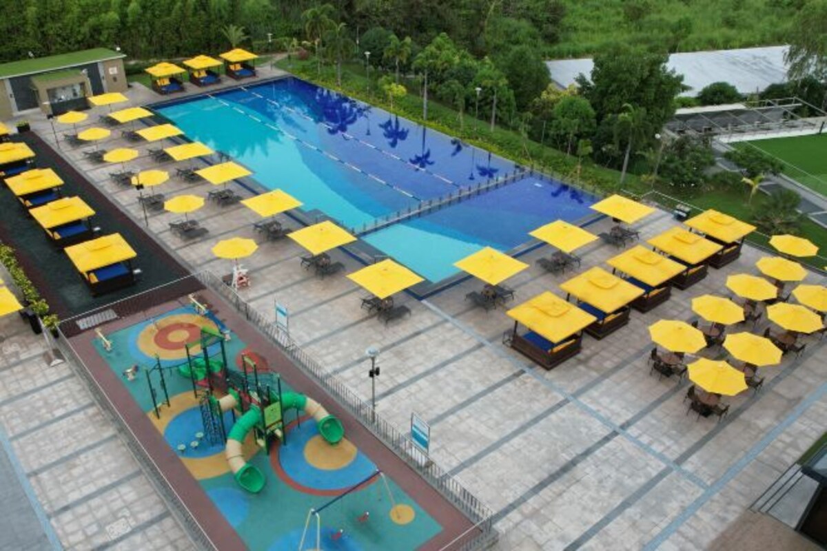 Piscina com guarda-sóis amarelos e espreguiçadeiras, cercada por vegetação.