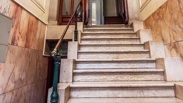 Uma escadaria de mármore com decoração de parede elaborada e corrimão de madeira.