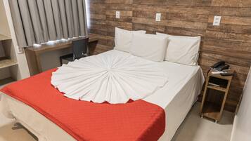 Cama bem arrumada com manta vermelha, cabeceira de madeira e mesa de cabeceira com telefone e controle remoto.