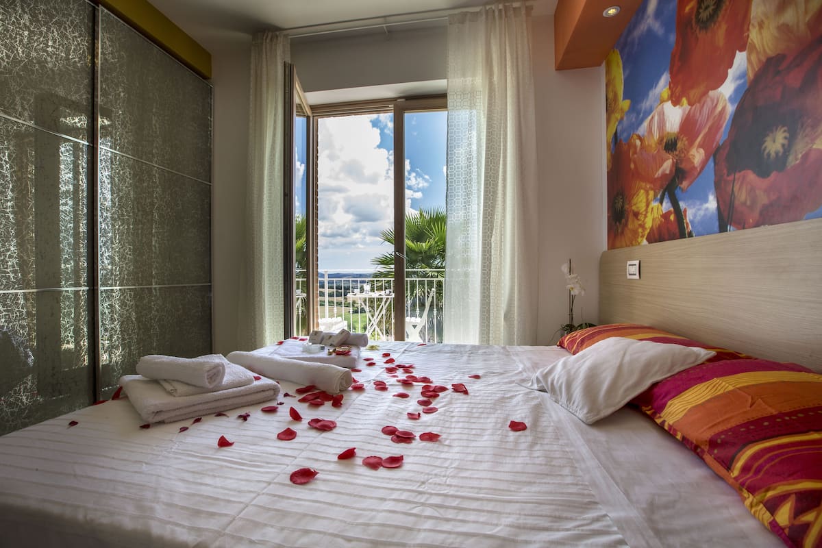 Quarto de hotel com cama, toalhas e pétalas de rosa.