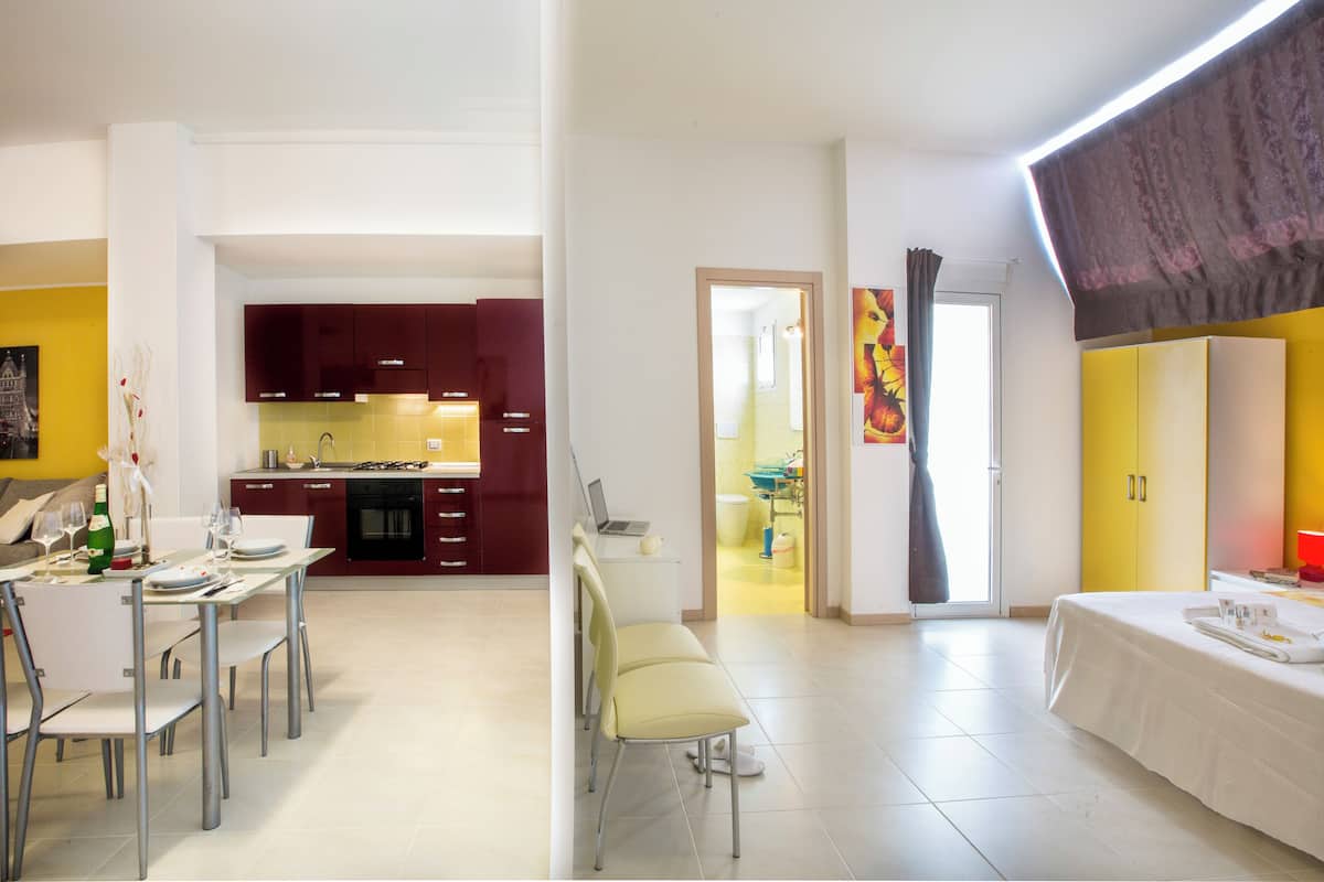 Quarto de hotel moderno com área de refeições, cozinha e uma cama grande.