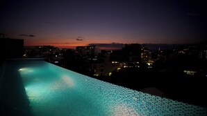 Vista noturna de uma piscina com luzes da cidade ao fundo.