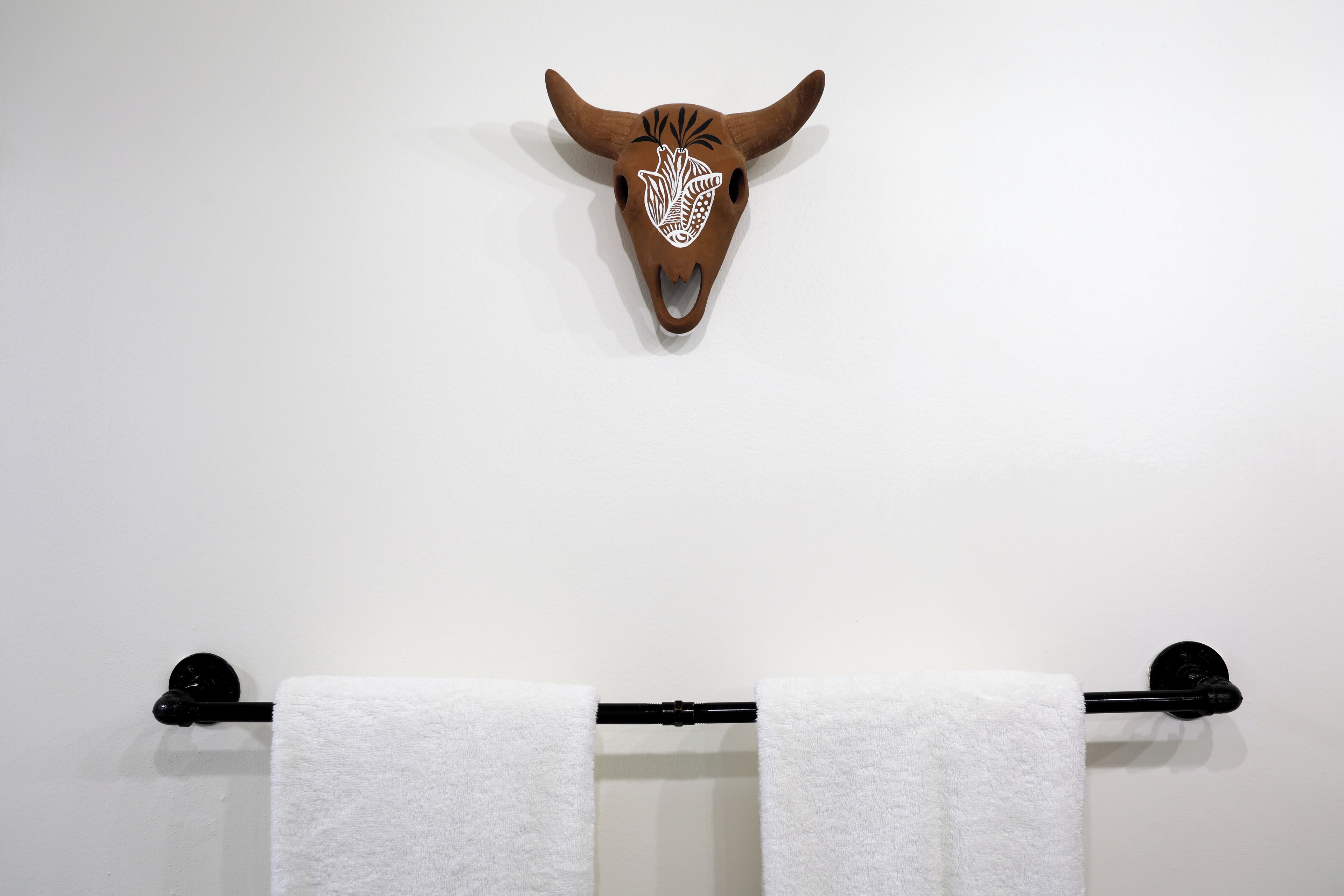 Casa de banho com barra de toalhas com duas toalhas brancas e um crânio de touro decorativo fixado na parede.