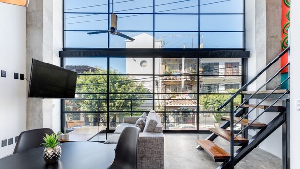 Uma sala de estar moderna com uma janela grande, uma TV de tela plana, uma mesa de jantar e uma escada.