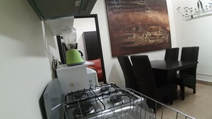 Uma cozinha com fogão a gás, liquidificador e mesa de jantar com cadeiras.